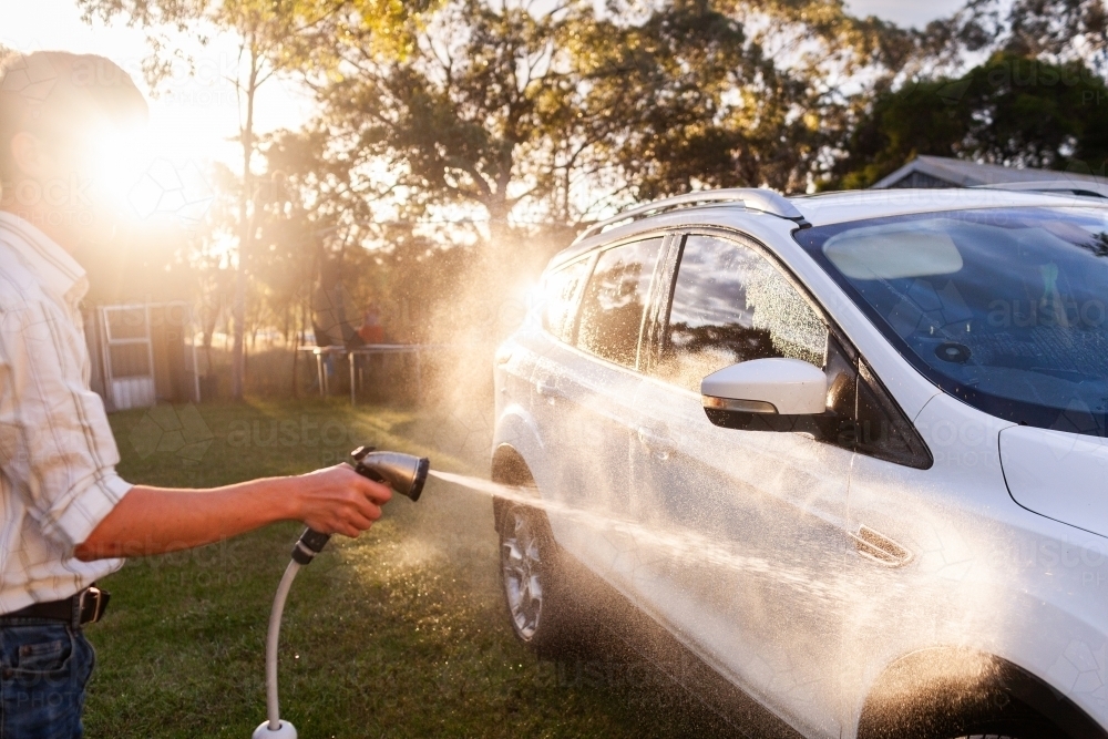 Image of Teen boy washing car spraying vehicle with water in golden ...