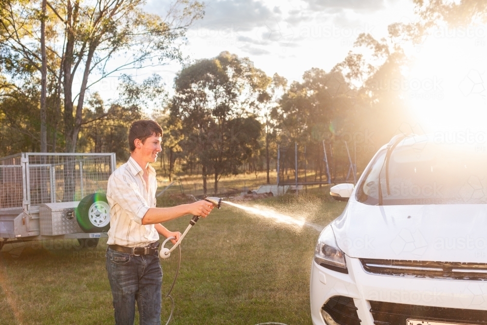 Image of Teen boy washing car spraying vehicle with water in golden ...