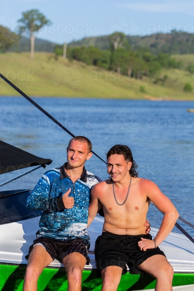Image of teen cousins sitting together on boat at lakeside - Austockphoto