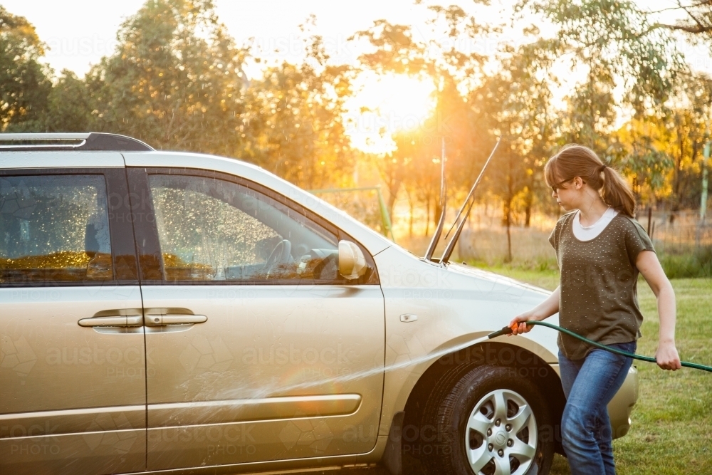 Image of Teen girl hosing down car in the backyard - Austockphoto