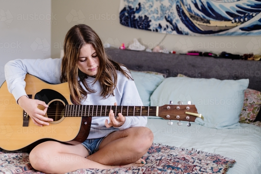 Image of teen girl playing guitar in her bedroom - Austockphoto