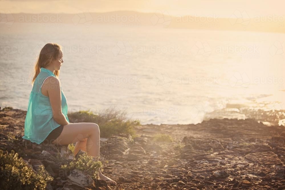 Image of Teen girl reflecting at the beach at sunset - Austockphoto