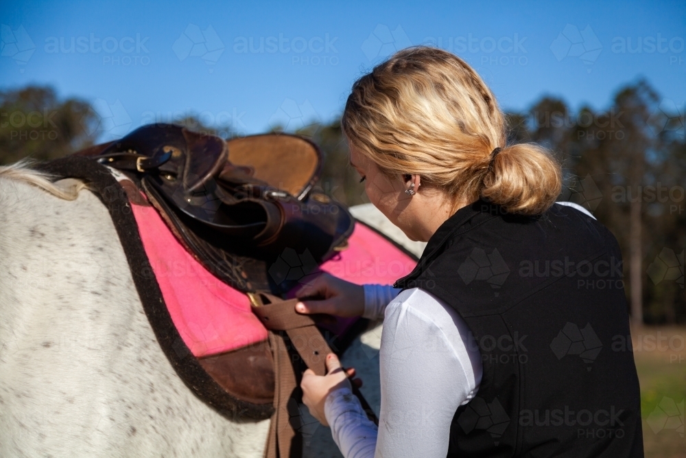Image of Teen girl saddling up her horse - Austockphoto
