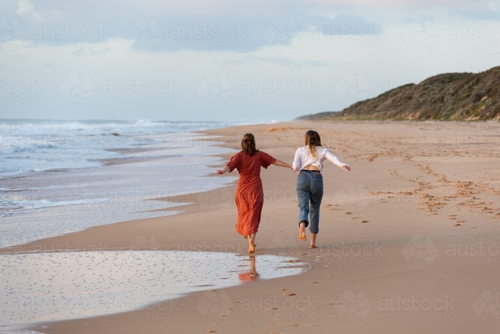 Image of teen girls running on beach hand in hand - Austockphoto