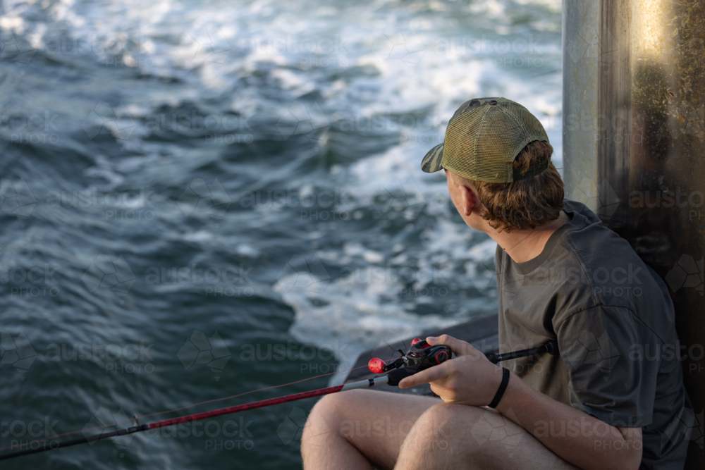 Image of Teenage boy fishing off jetty looking out over the water ...
