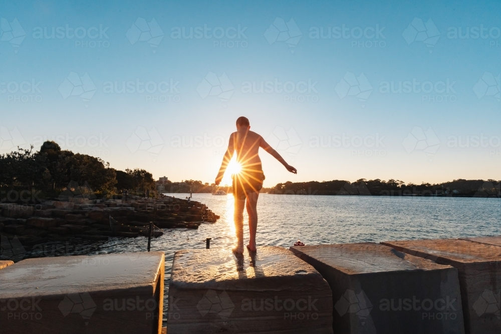 Image of Teenage boy jumping from ledge into water in bright setting ...