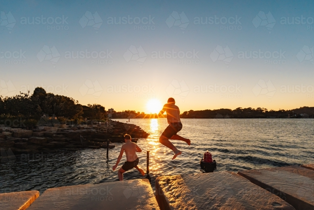 Image of Teenage boy jumping from ledge into water in bright setting ...