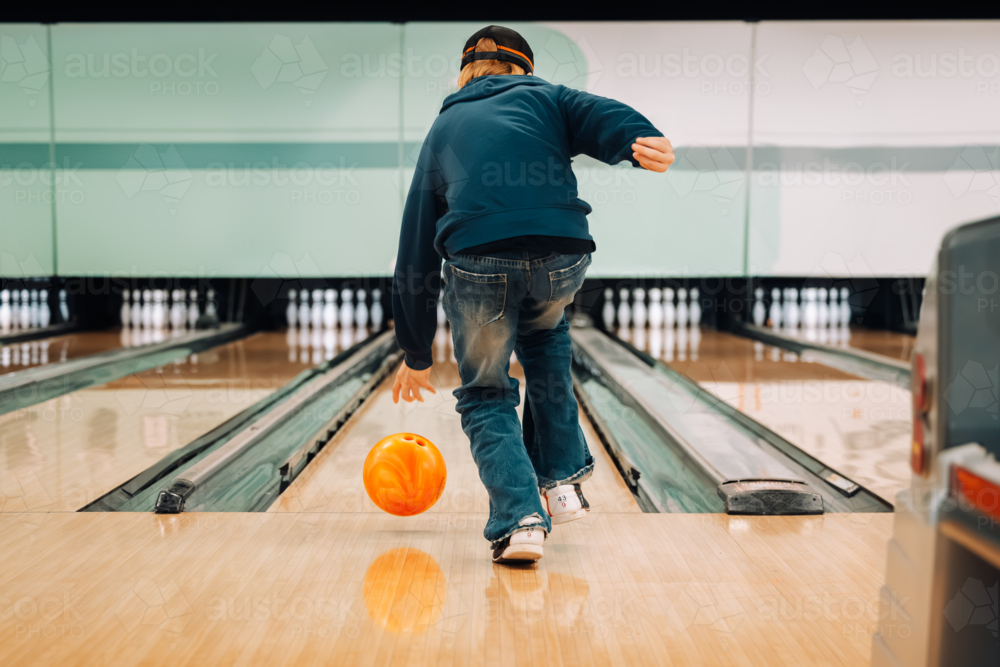 Image of Teenage boy mid-roll while ten pin bowling in brightly lit ...