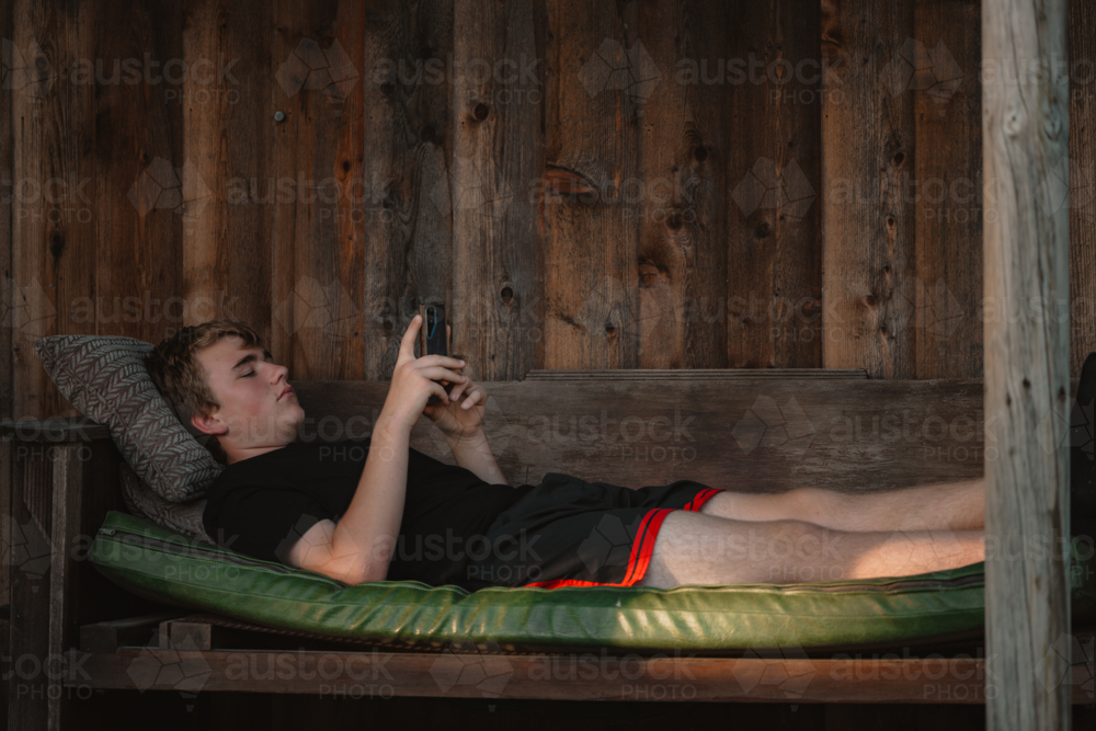 Image of Teenage boy relaxing on outdoor lounge using mobile phone ...
