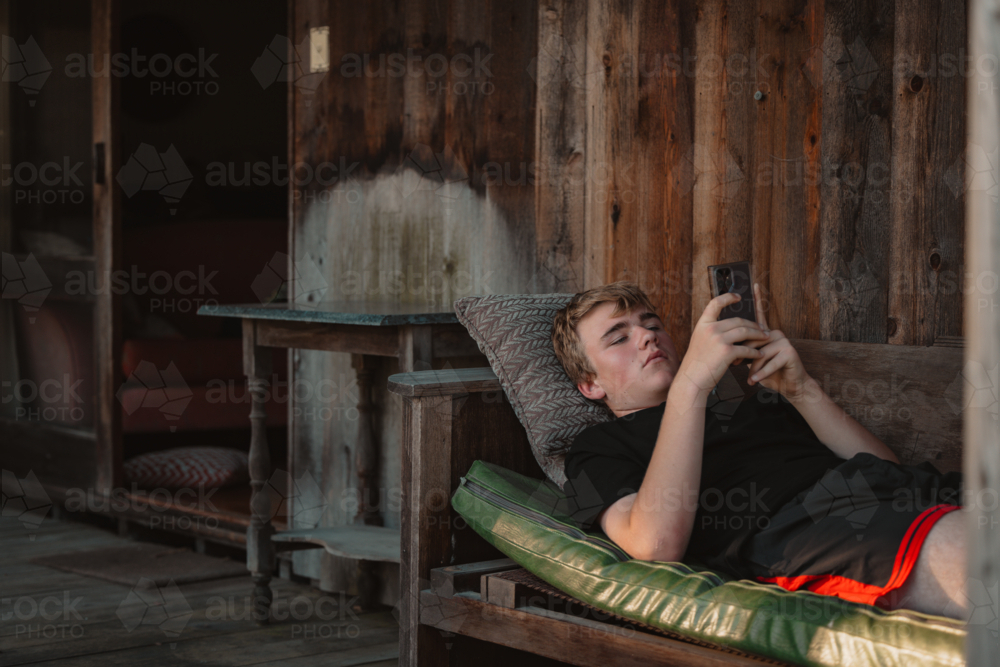Image of Teenage boy relaxing on outdoor lounge using mobile phone ...
