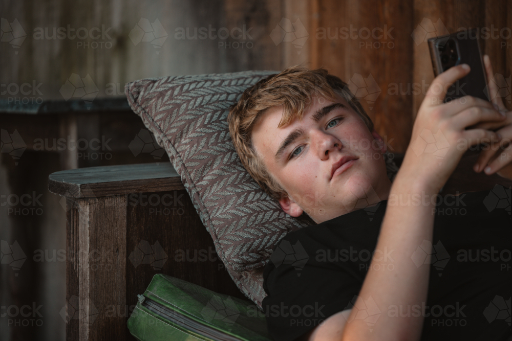 Image of Teenage boy relaxing on outdoor lounge using mobile phone ...