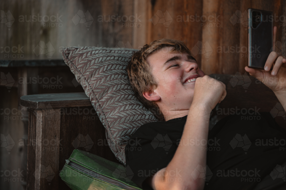Image of Teenage boy relaxing on outdoor lounge using mobile phone ...