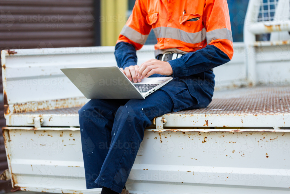 Image of teenaged trainee tradie apprentice working on laptop in back ...