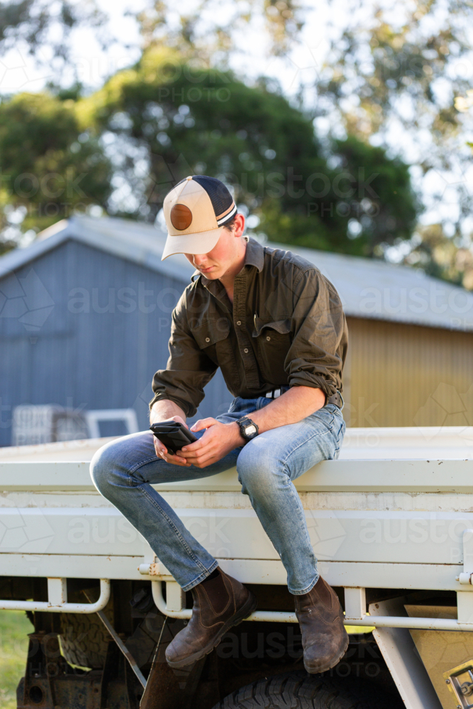 Image of teenaged young man sitting on ute tray using mobile phone ...