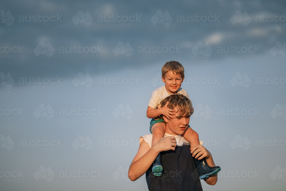Image of Teenager giving happy little boy a shoulder ride with a blue ...