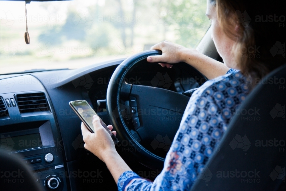 Image of Texting and driving, young woman driver in car with mobile ...