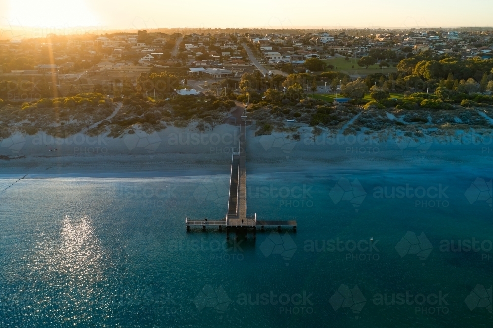 Image of The sun rising over the horizon behind water and jetty at ...
