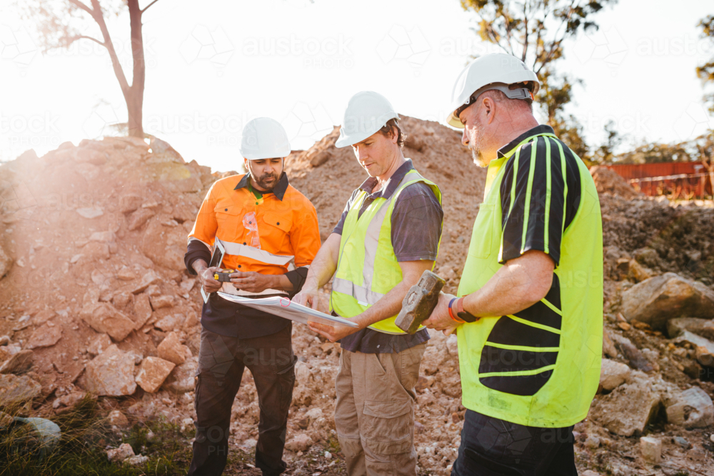 Image of Three builders in hardhats looking at the blueprints at ...