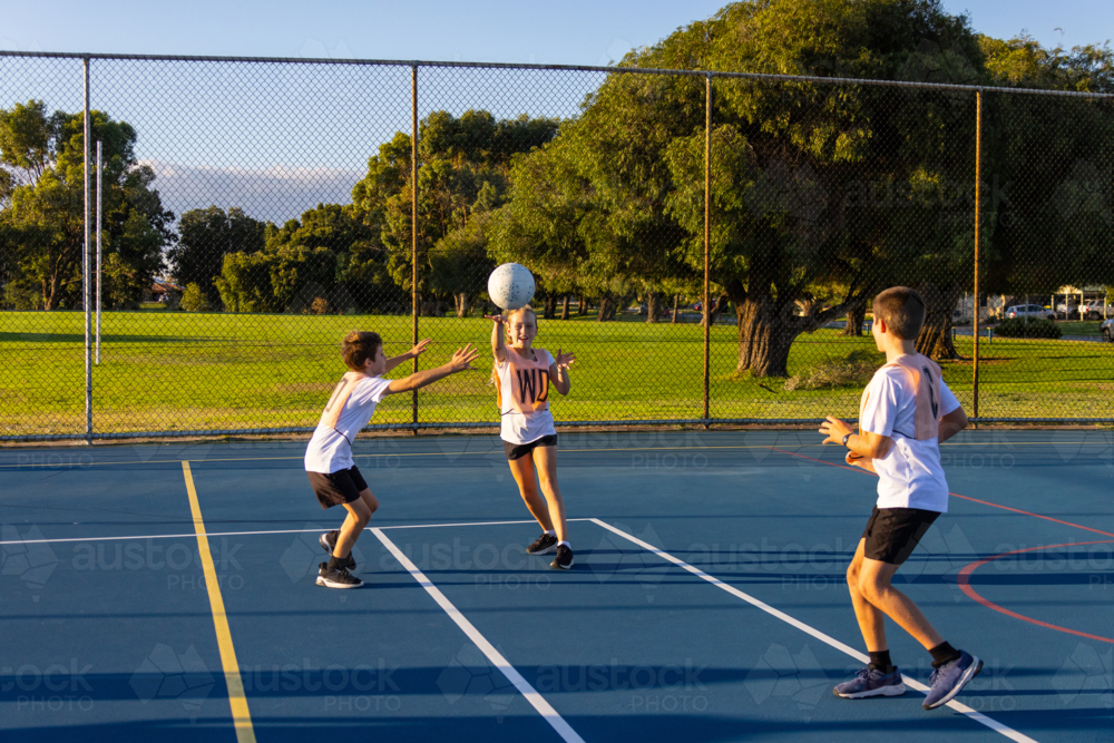 Image of three children doing a netball training drill on blue playing ...