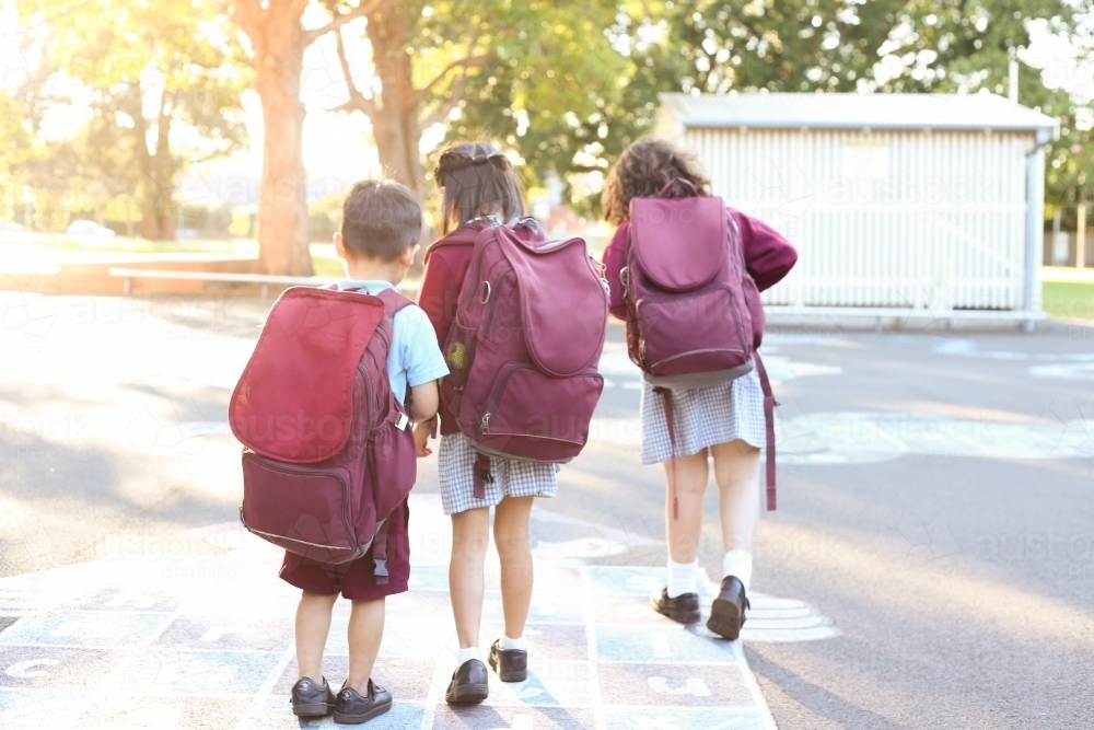 Image of Three children leaving school with their backs to the camera ...