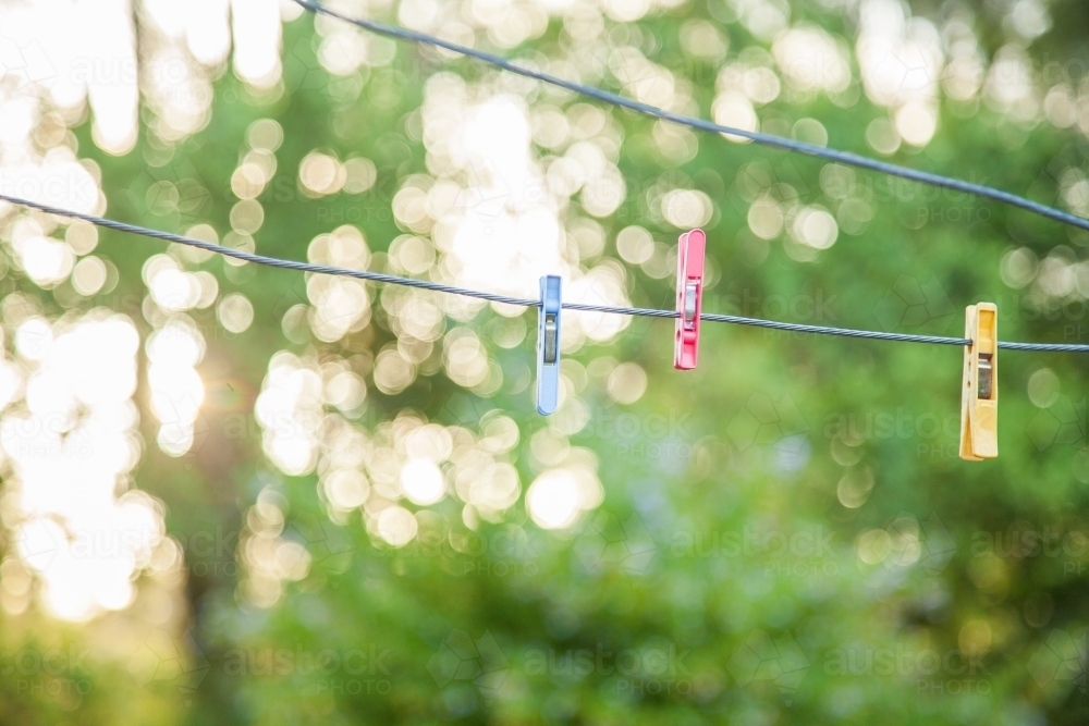 Image of Three coloured clothes pegs hanging on an empty washingline ...