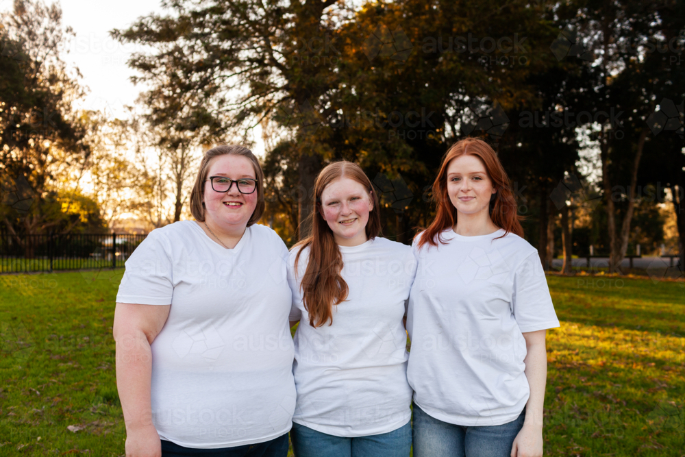 Image of Three happy sisters standing together outdoors in green ...
