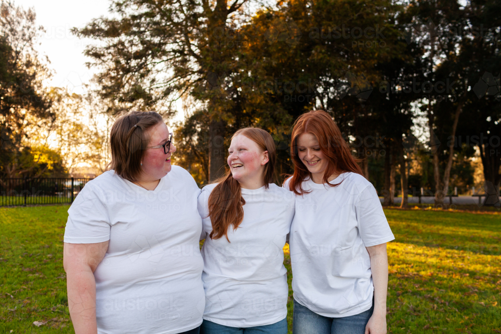 Image of Three happy sisters standing together outdoors in green ...