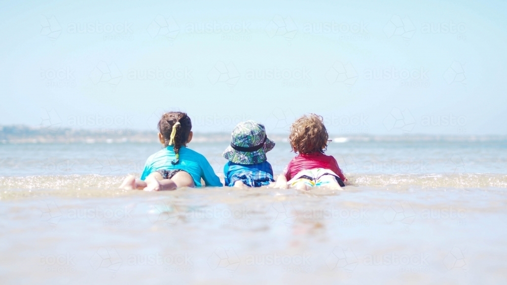 Image of Three kids lying in the surf at the beach - Austockphoto