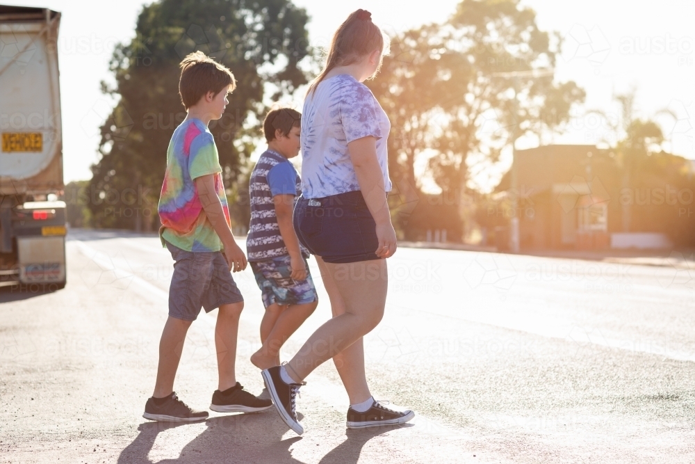 Image of Three kids walking across a road with a truck in the ...