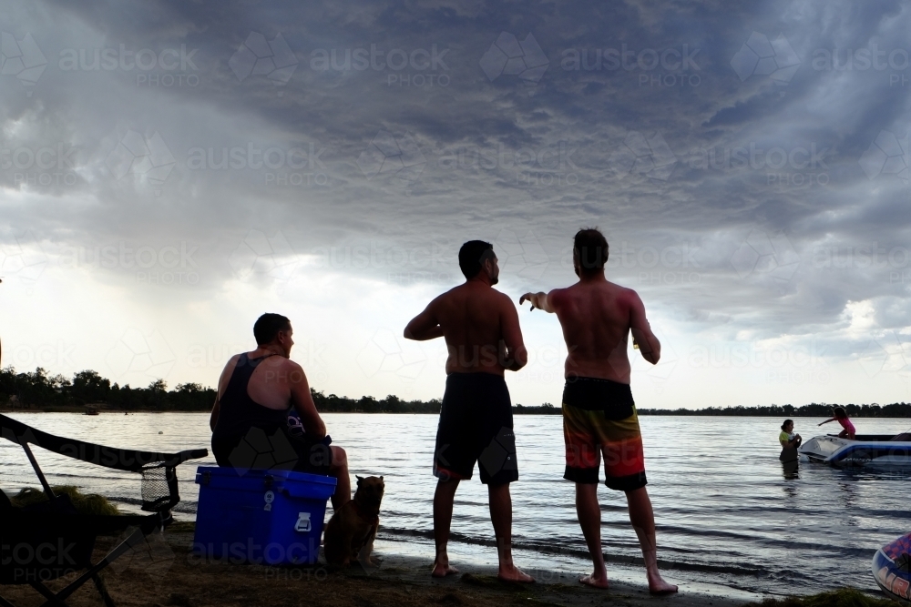 Image of Three men standing watching storm approaching over lake ...