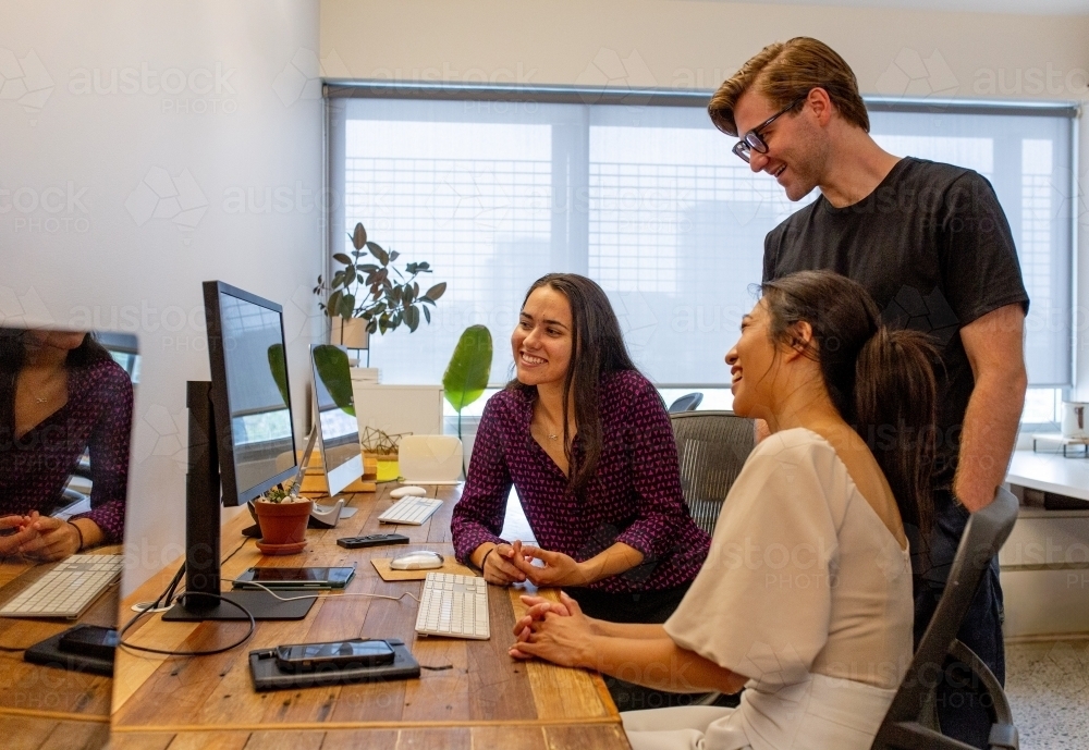 Image of Three office workers looking together at a computer screen in ...