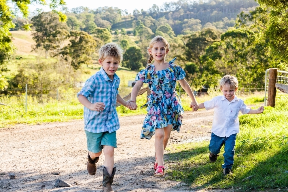 Image of Three siblings running down the farm driveway, playing a game ...