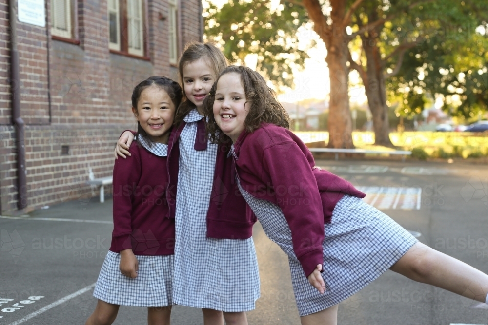 Image of Three smiling girls hugging outside their school - Austockphoto