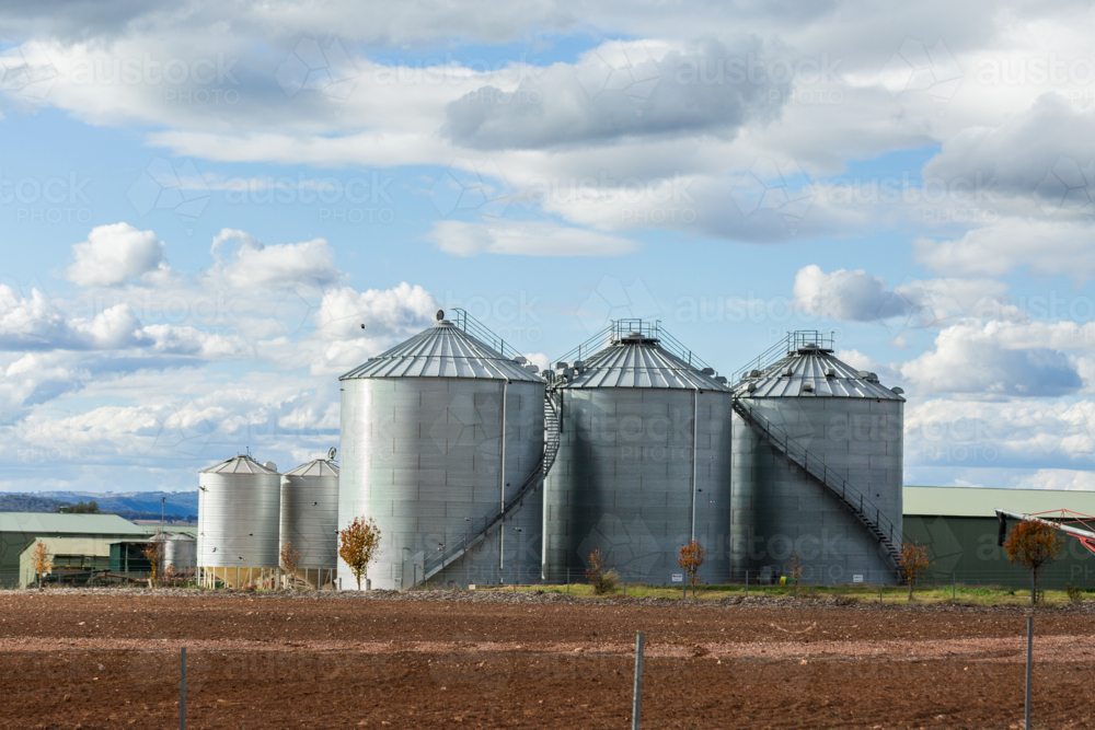 Image of three storage silos in farm paddock with red tilled dirt ...