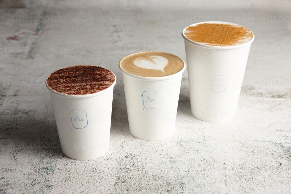 Image of Three takeaway coffees lined up on bench - Austockphoto