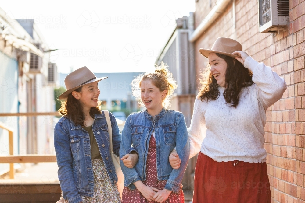 Image of Three teen friends walking down alleyway laughing together ...