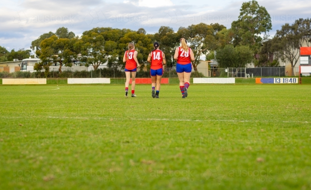 Image of three young female footballers jogging across football oval ...