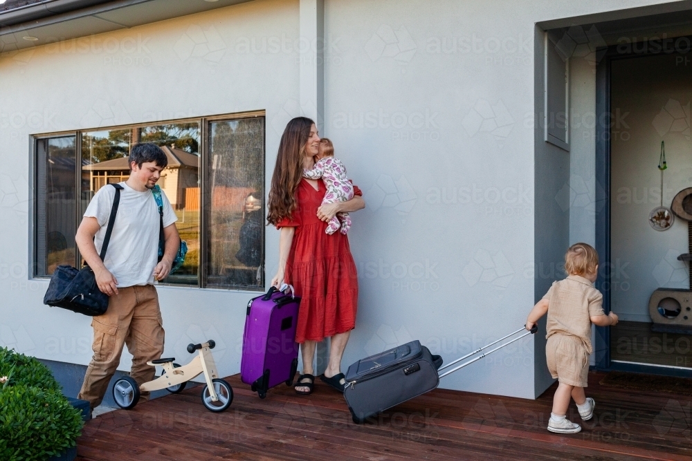 Image of Toddler boy helping family carry suitcase of luggage inside at ...