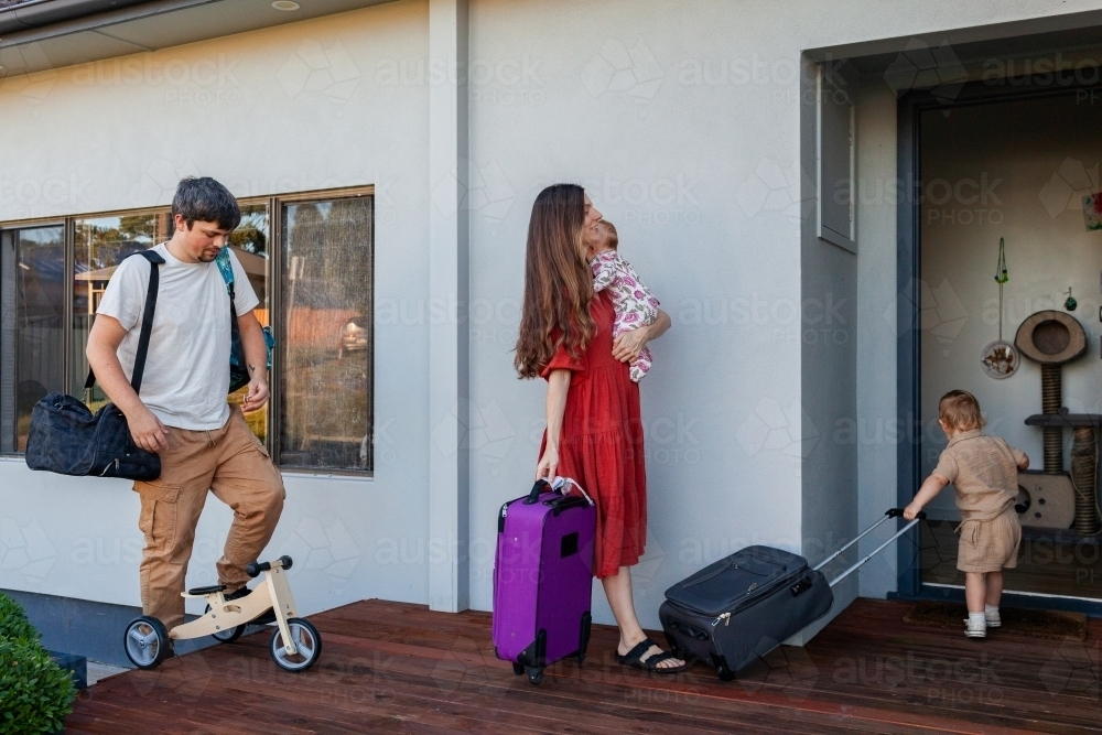 Image of Toddler boy helping family carry suitcase of luggage inside at ...