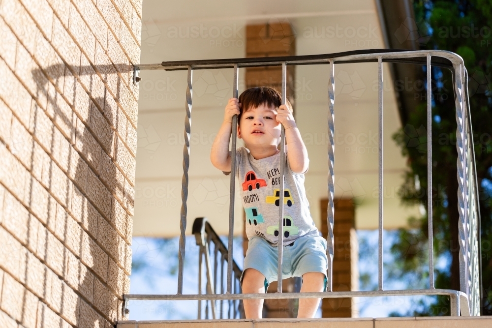 Image of Toddler boy looking through railing of balcony - Austockphoto