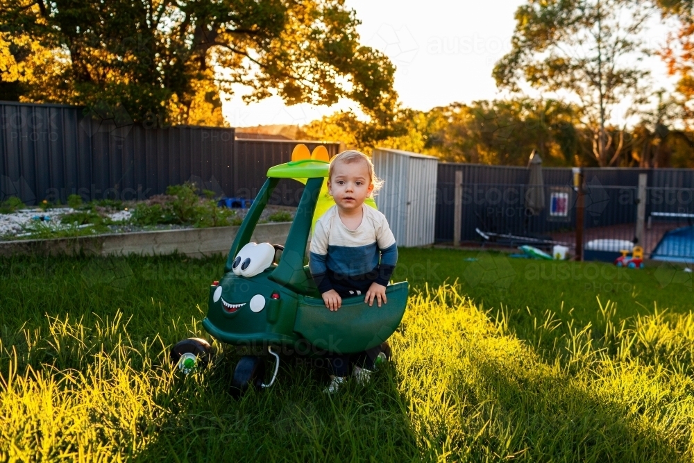 Image of toddler boy playing with green toy ride in car in backyard ...