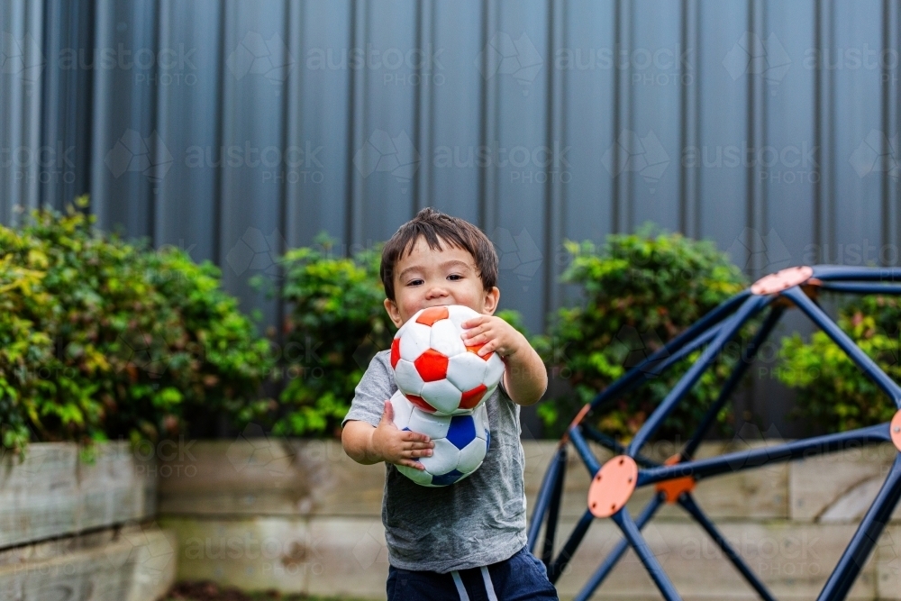 Image of toddler carrying balls around in suburban backyard - Austockphoto