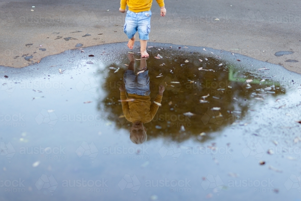 Image of toddler child getting his feet wet reflected in shallow puddle ...