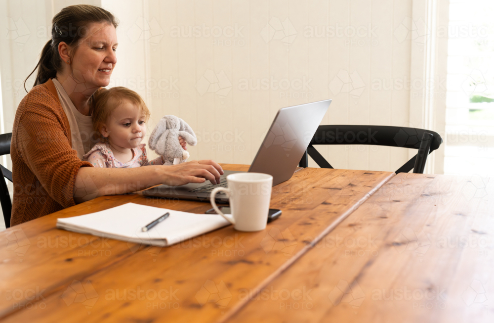 Image of Toddler daughter sitting on mothers lap while working on her ...