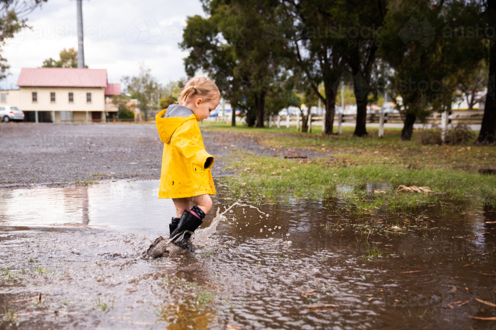 Image of toddler girl in yellow raincoat marching through a puddle ...