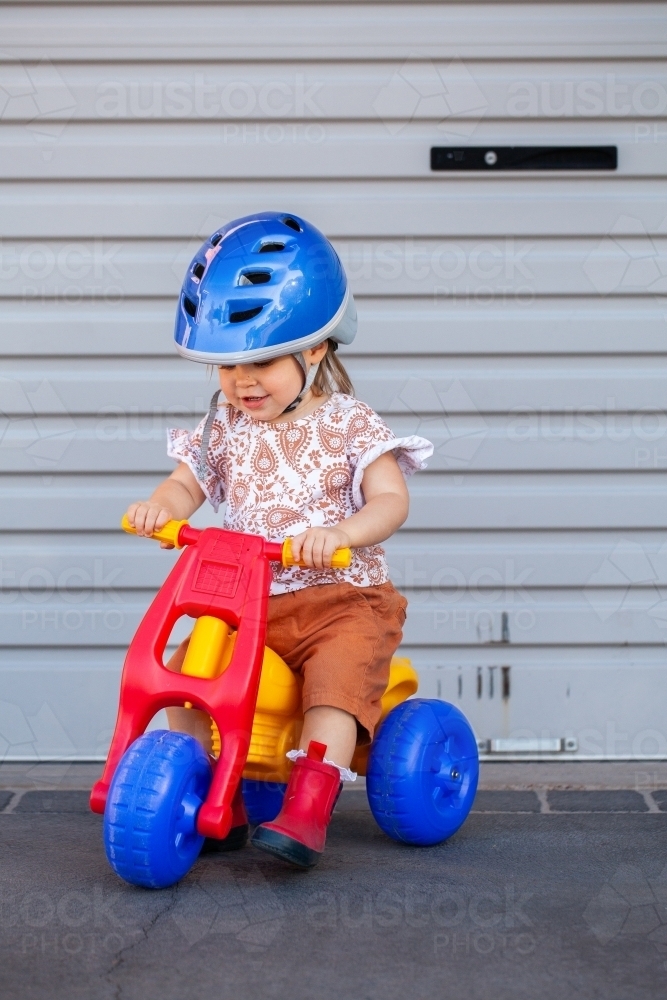 Image of Toddler girl riding colourful tricycle outside garage ...