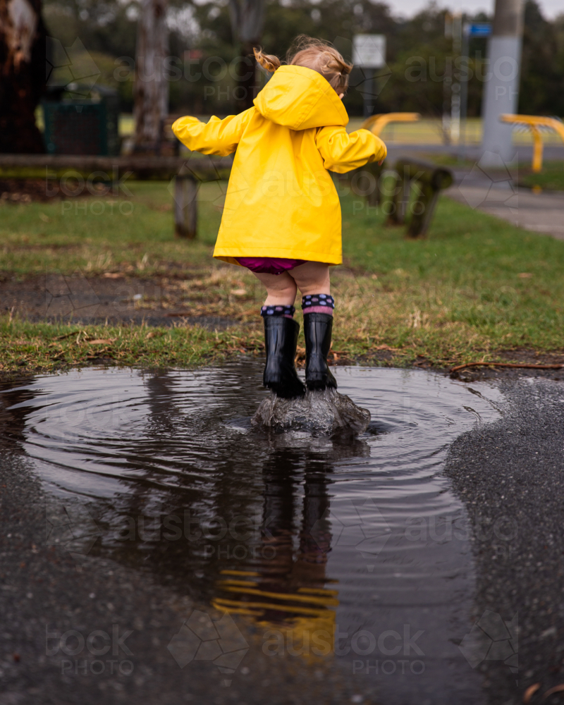 Image of toddler in yellow raincoat jumping in a dark puddle - Austockphoto