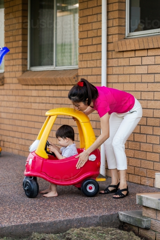 Image of Toddler playing in push car on back porch with Vietnamese mum ...