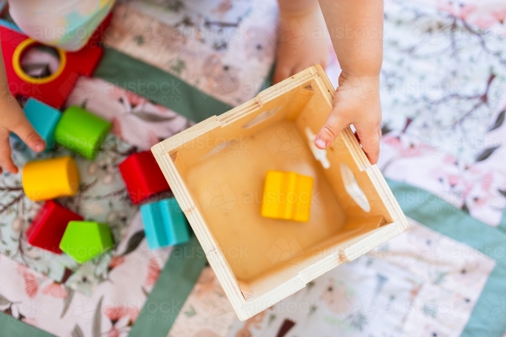 Image of Toddler playing with coloured shapes in wooden shape sorter ...