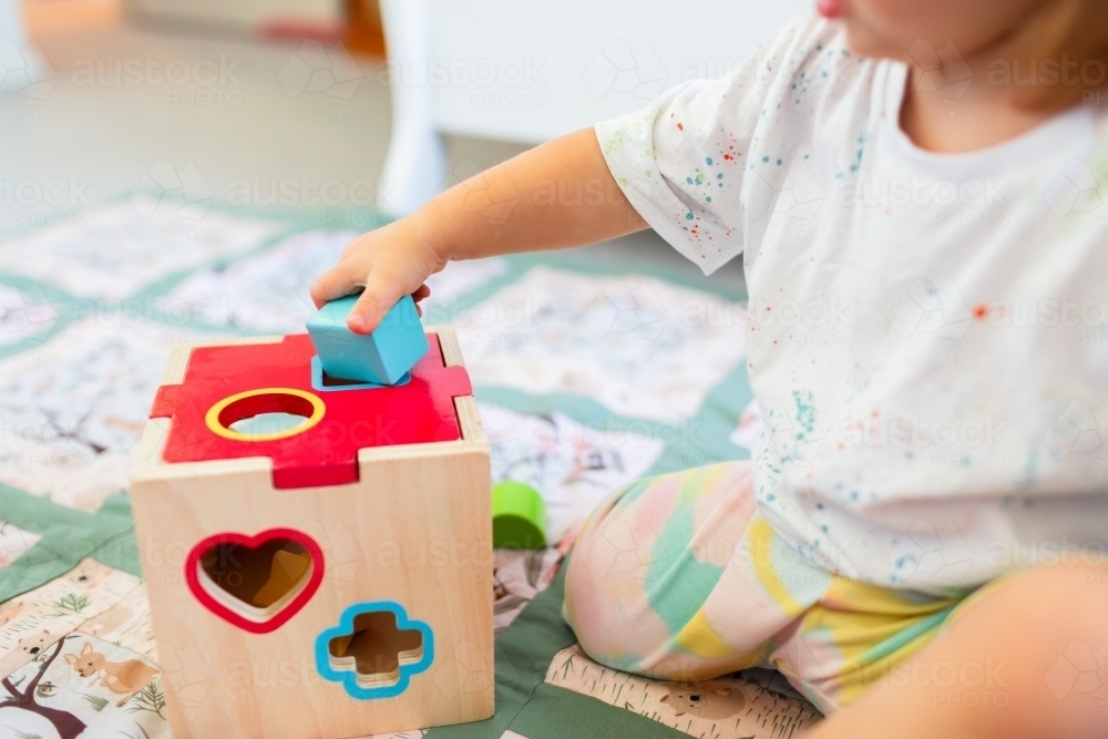 Image of Toddler posting coloured shapes into wooden shape sorter box ...